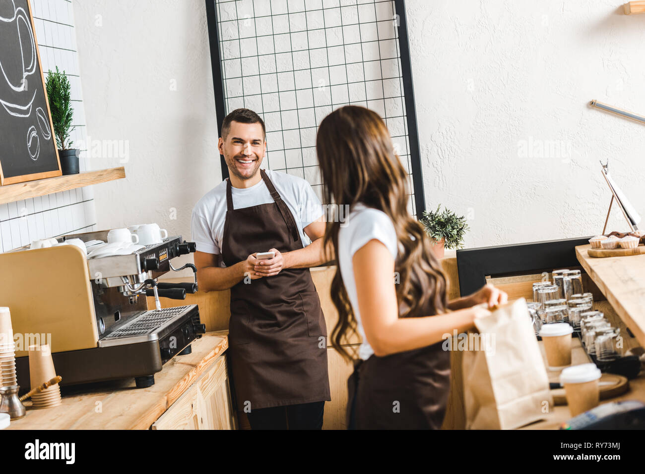 selective focus of handsome cashier with smartphone and barista ...