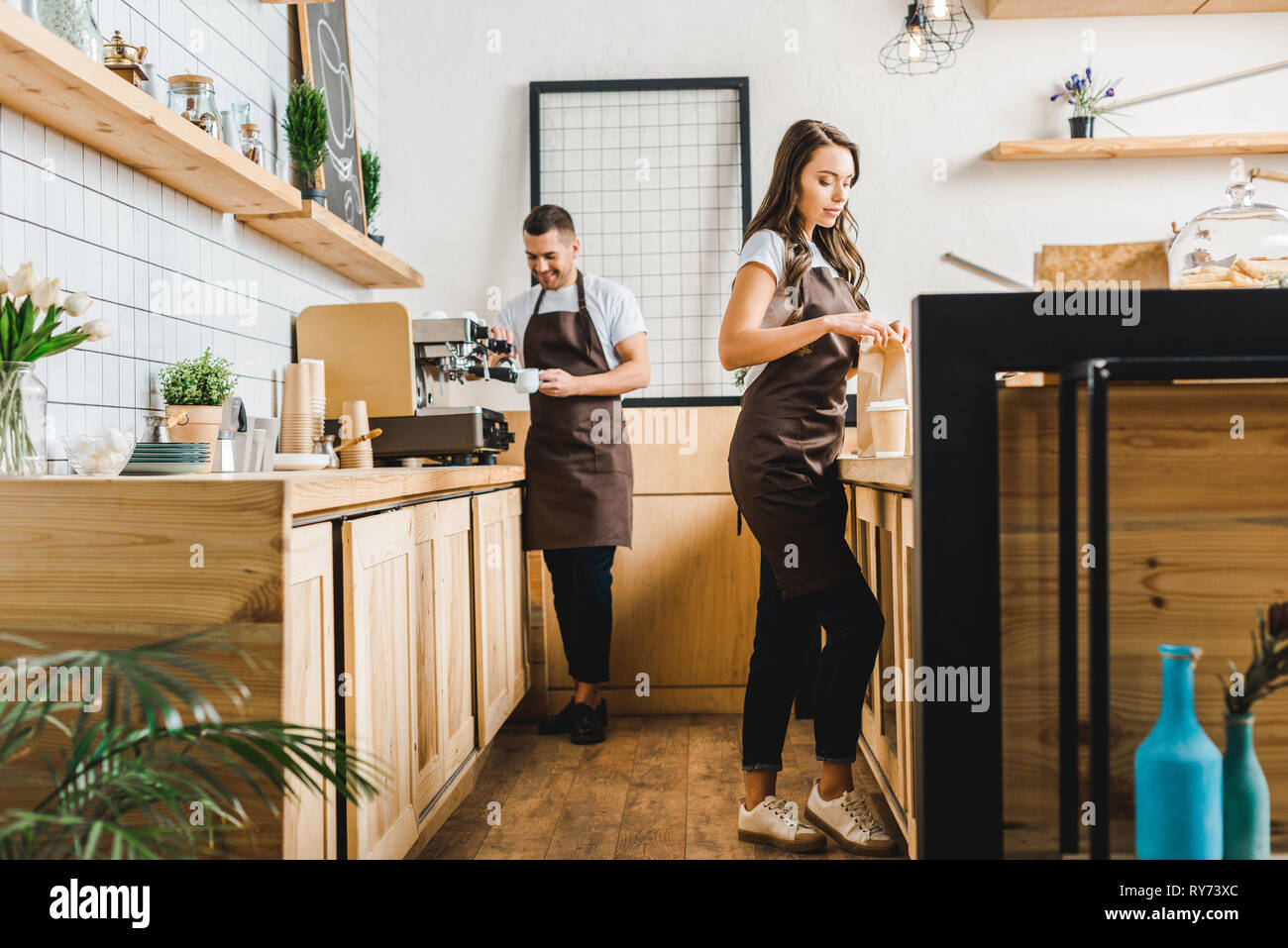 attractive cashier with paper bag and barista making coffee behind bar ...