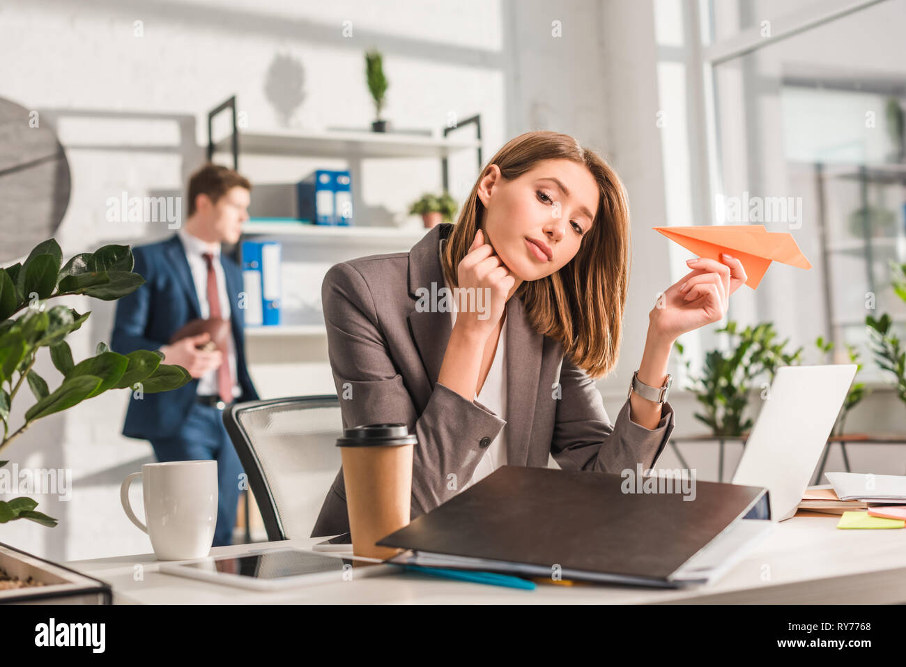 tired businesswoman holding paper plane near laptop with coworker on ...