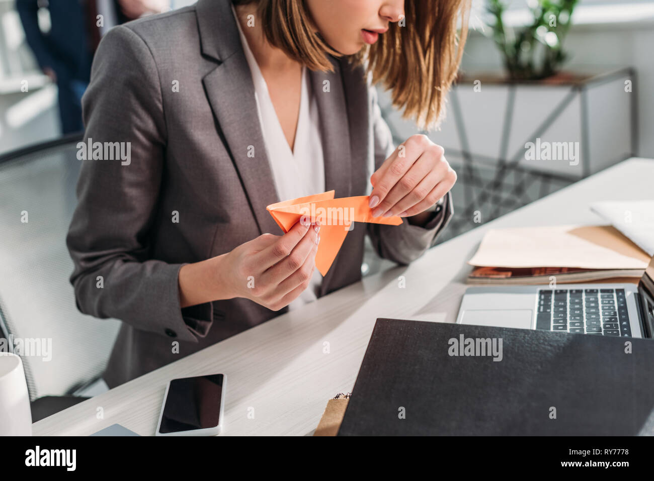 cropped view of surprised businesswoman holding paper plane and looking ...