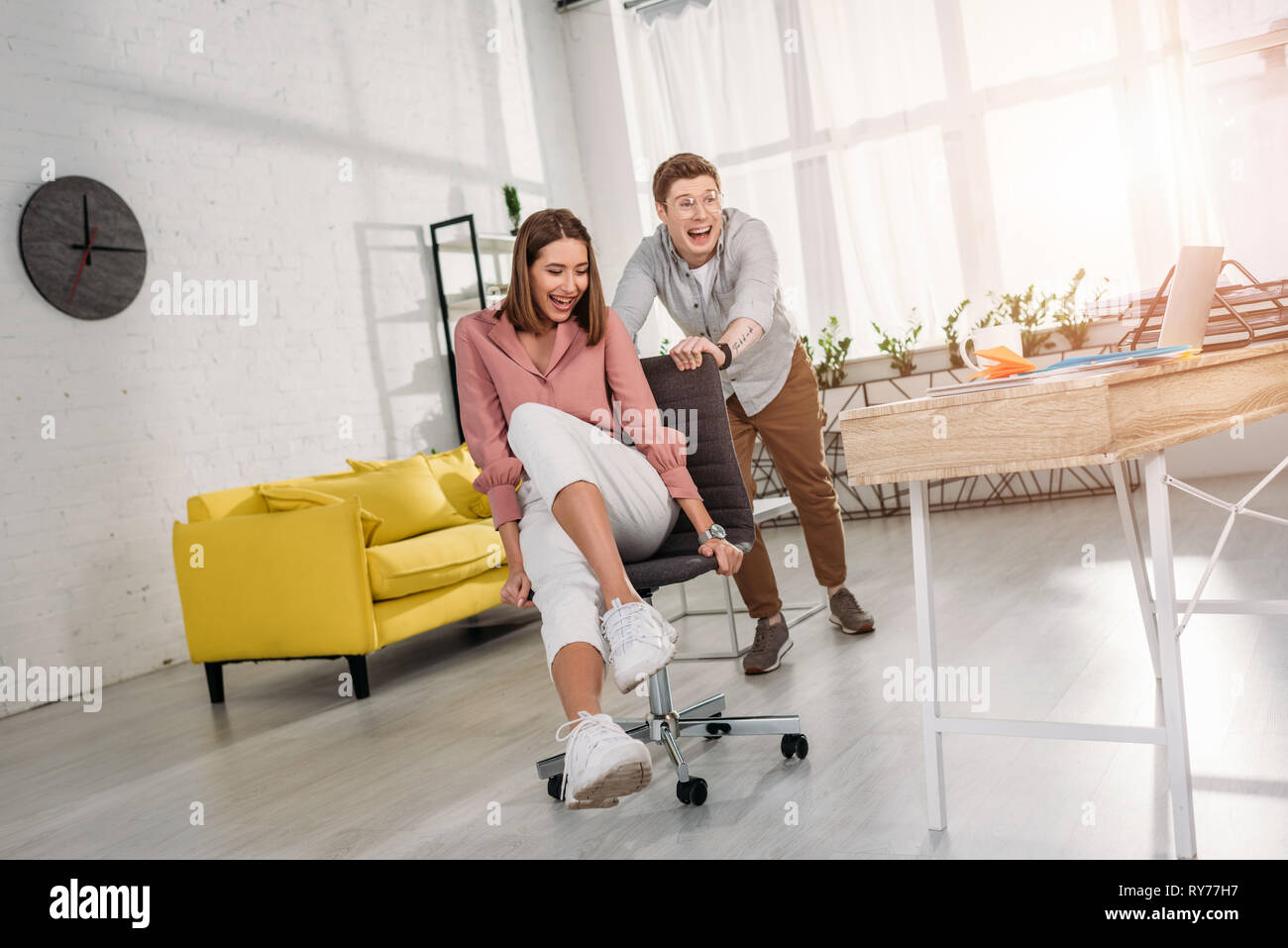 cheerful man smiling while pushing chair of happy girlfriend Stock ...