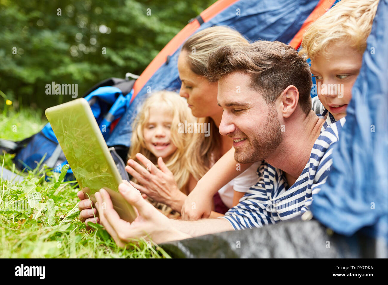 Family in tent at camping vacation looks together on tablet computer ...