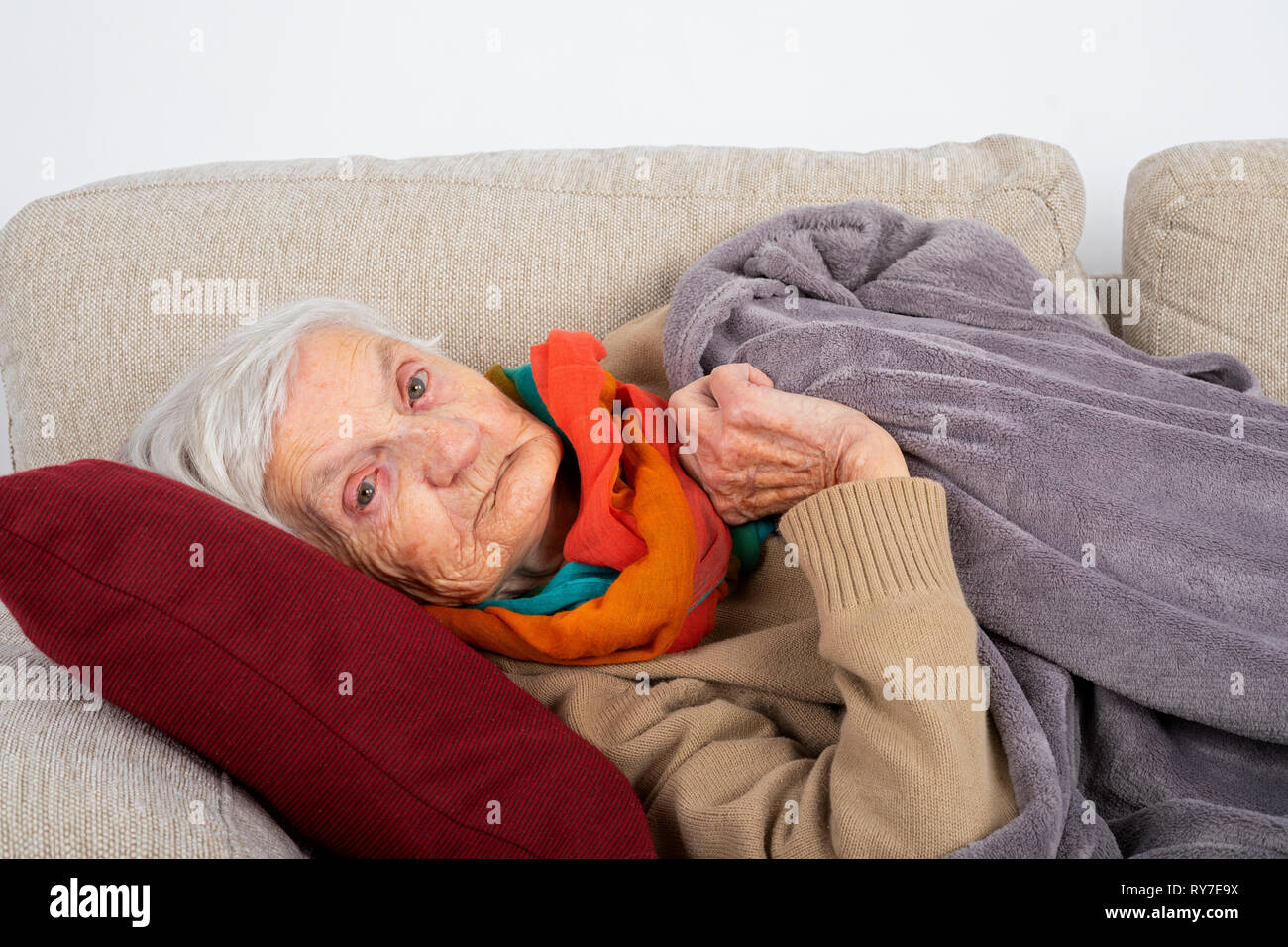 Close up picture of a sick old lady lying on the couch wrapped in a ...