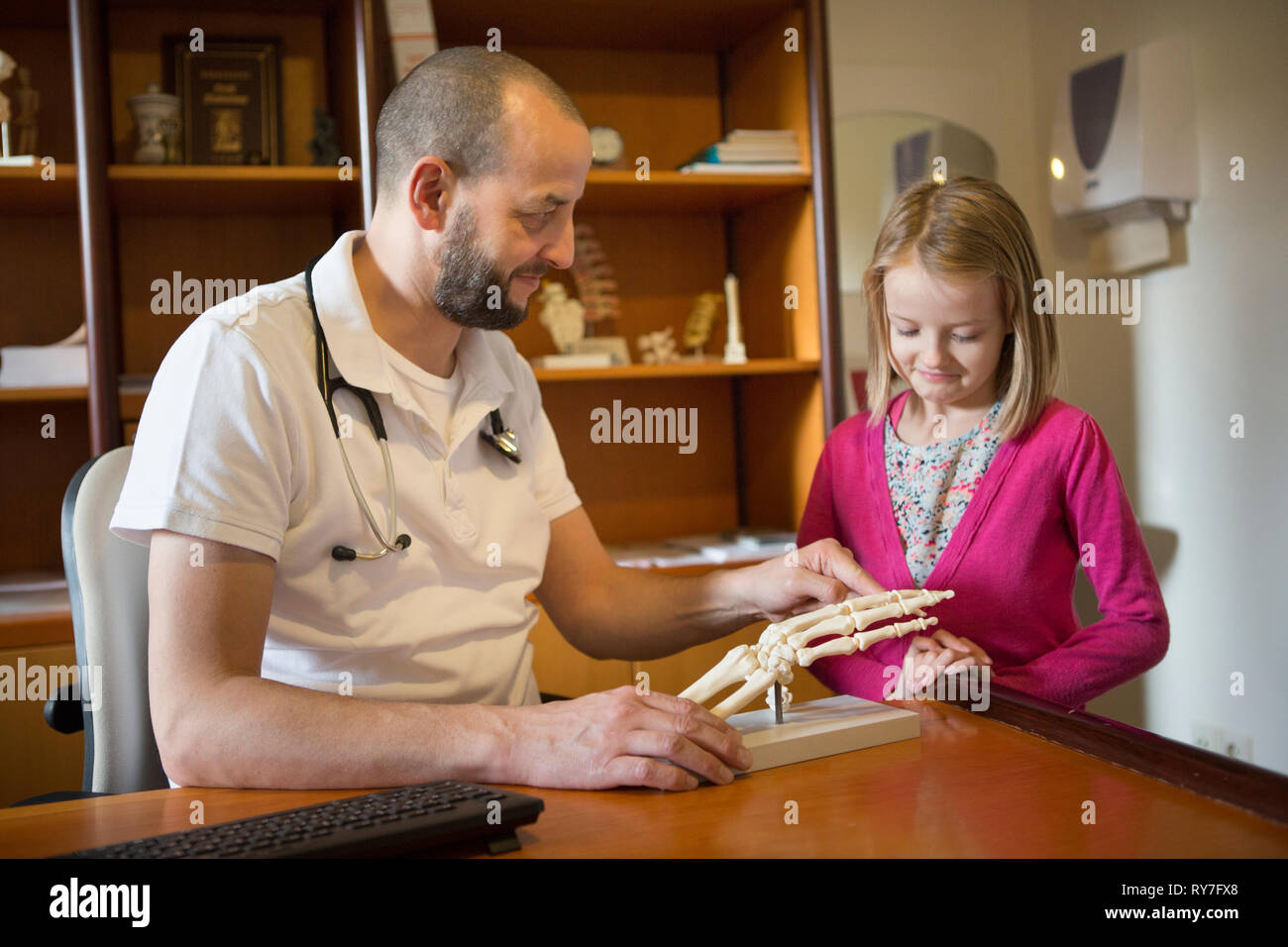 Doctor showing a child a replica model of the bones in a human hand ...