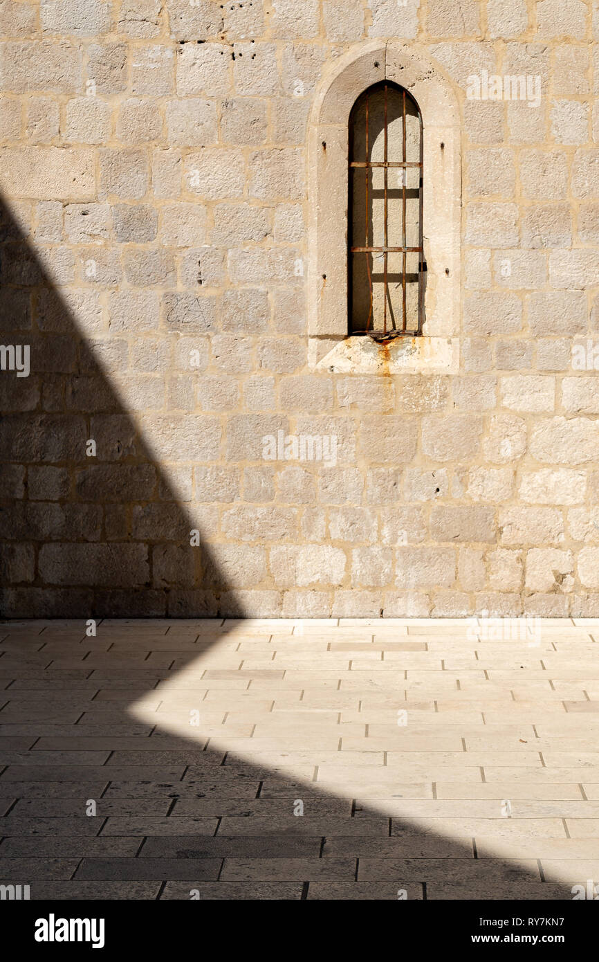 A small arched window with rusty bars across it and a shadow cast by ...
