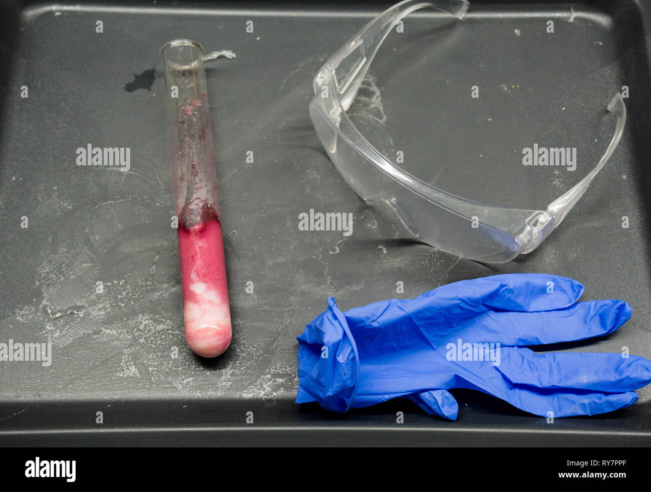 pair of blue lab gloves, protective goggles and flask with pink reagent ...