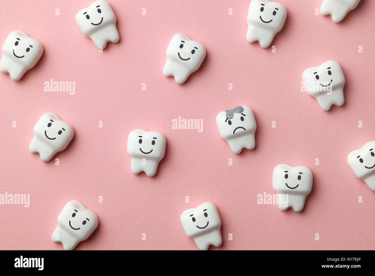 Healthy white teeth are smiling and tooth with caries is sad on pink ...