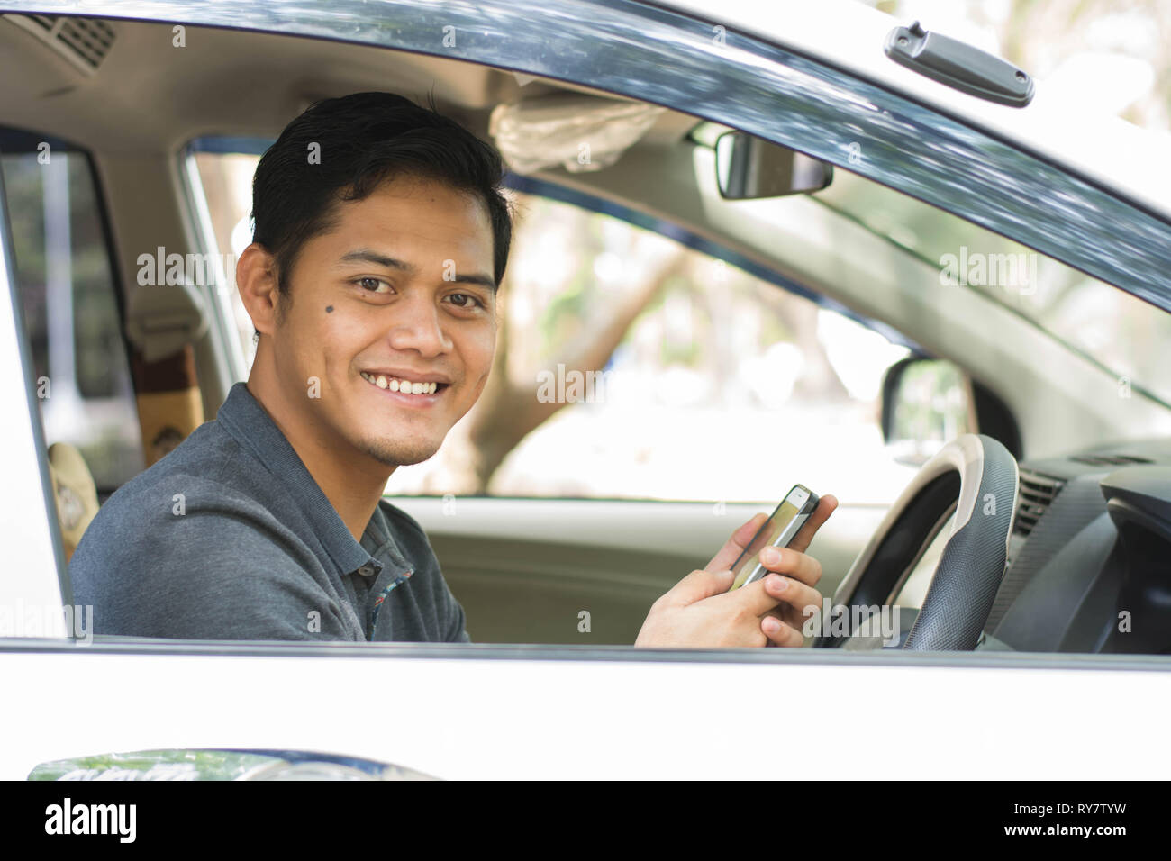 young attractive asian male using mobile phone and looking at camera ...