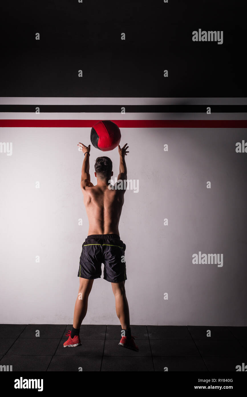Back view of athletic young shirtless guy jumping and tossing big ball ...