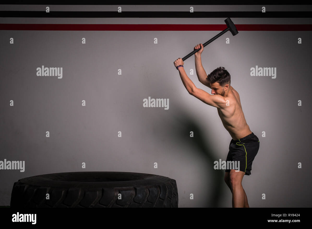 Shirtless guy concentrated in sportswear with hammer hitting on big ...
