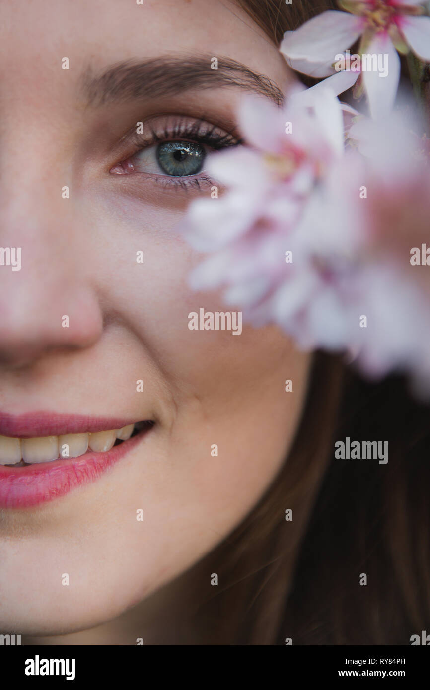 Crop face of young lady with blue eyes near branch of blooming wood ...