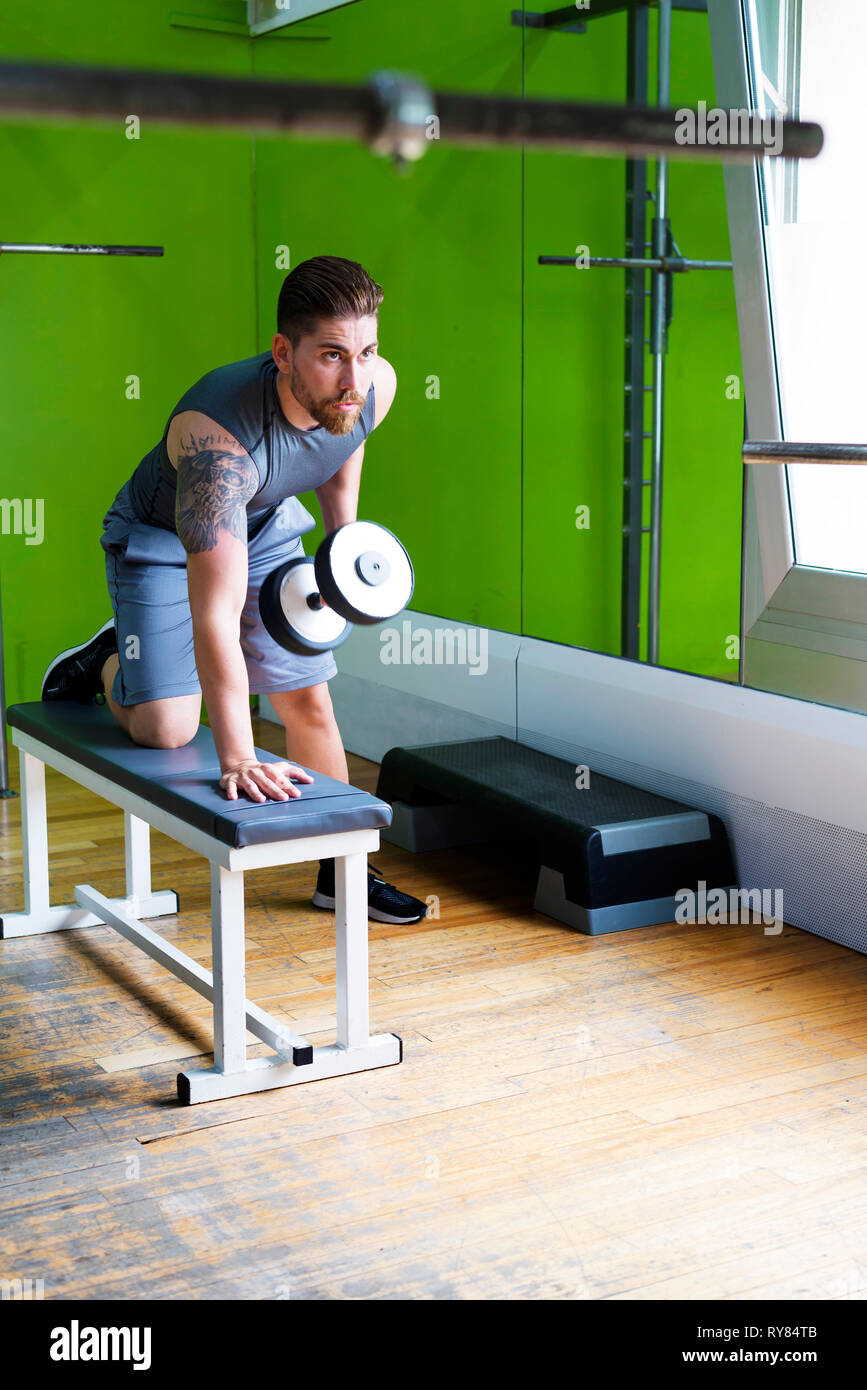 Confident man lifting dumbbell while leaning on seat against green wall ...