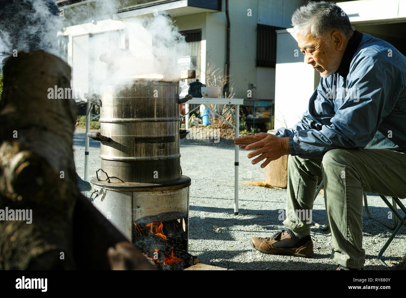An older Asian man warming himself up by the campfire Stock Photo - Alamy