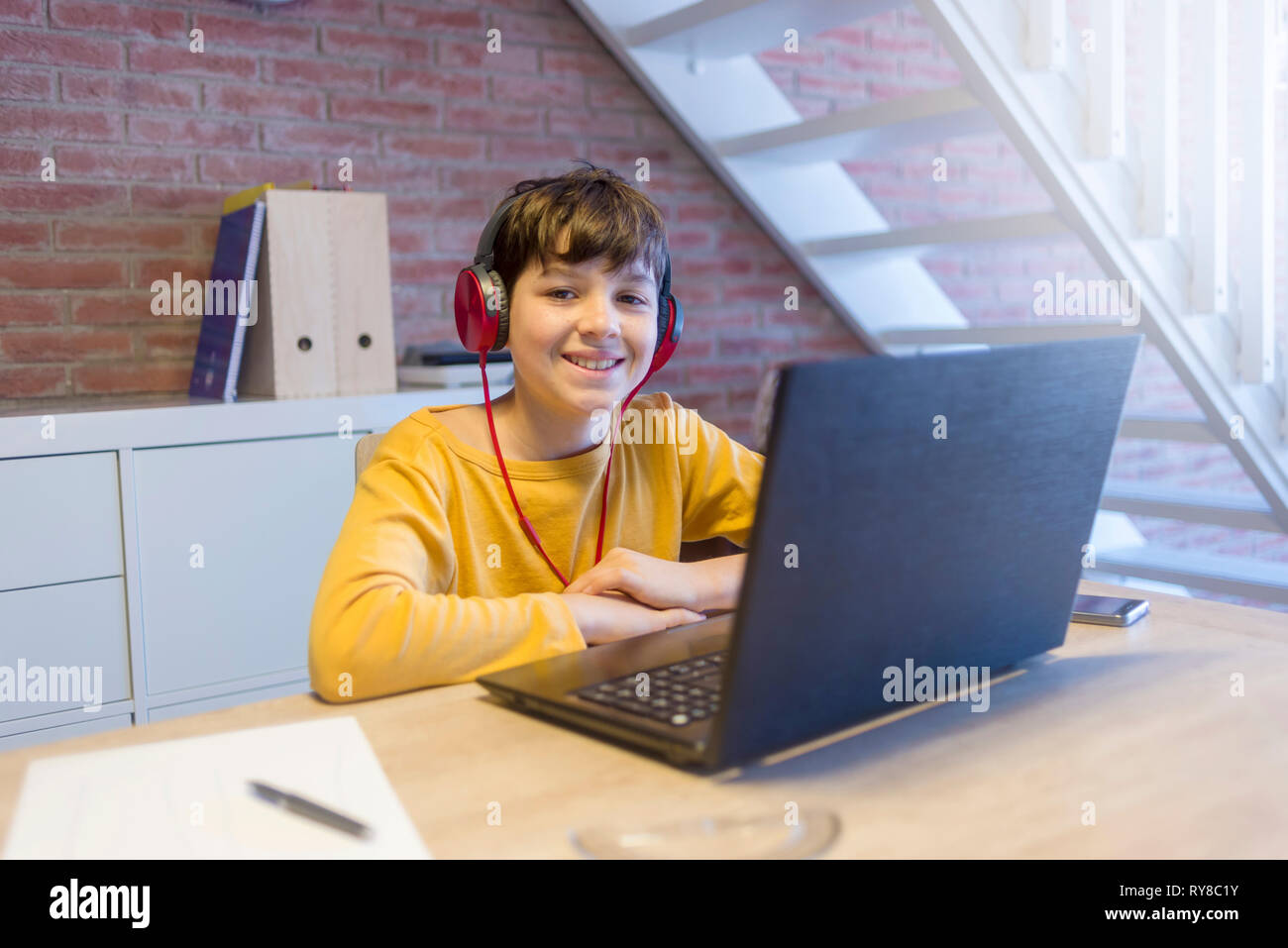 Portrait of smiling boy using headphones and laptop computer while ...