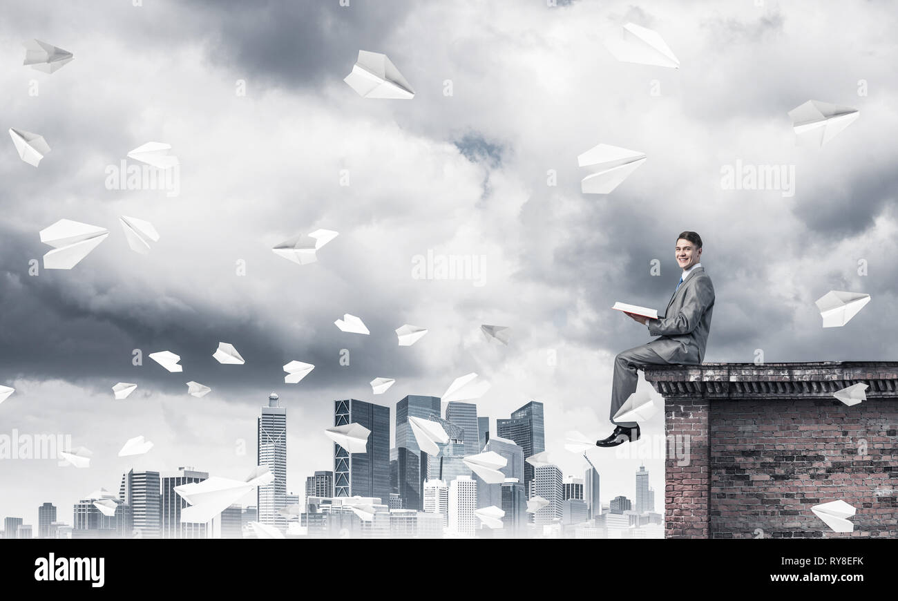 Man on roof edge reading book and cityscape at background Stock Photo ...