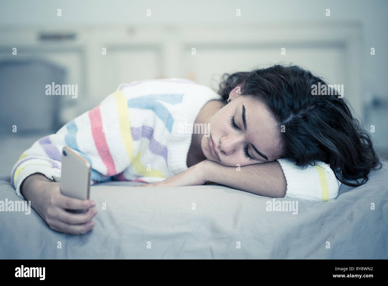 Closeup of young beautiful bored girl on bed using mobile phone. Tired ...