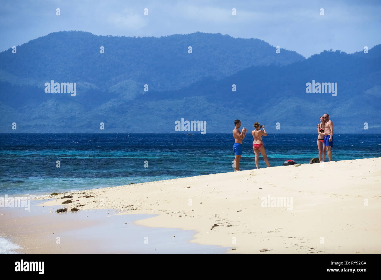 European tourist couples taking vacation photos on white sand beach ...