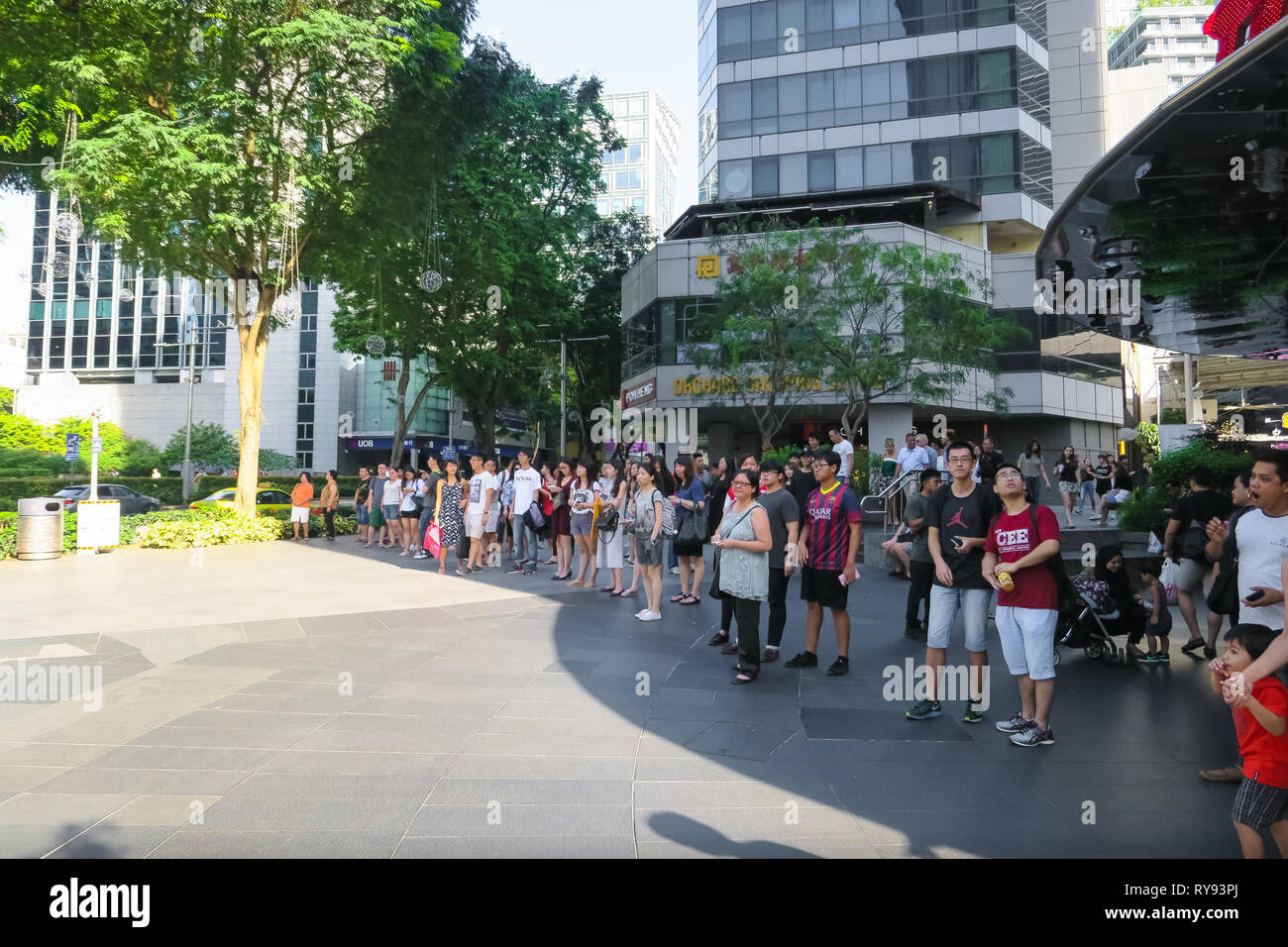 Crowd of Asian pedestrians avoiding the sun, waiting in the shade for a ...
