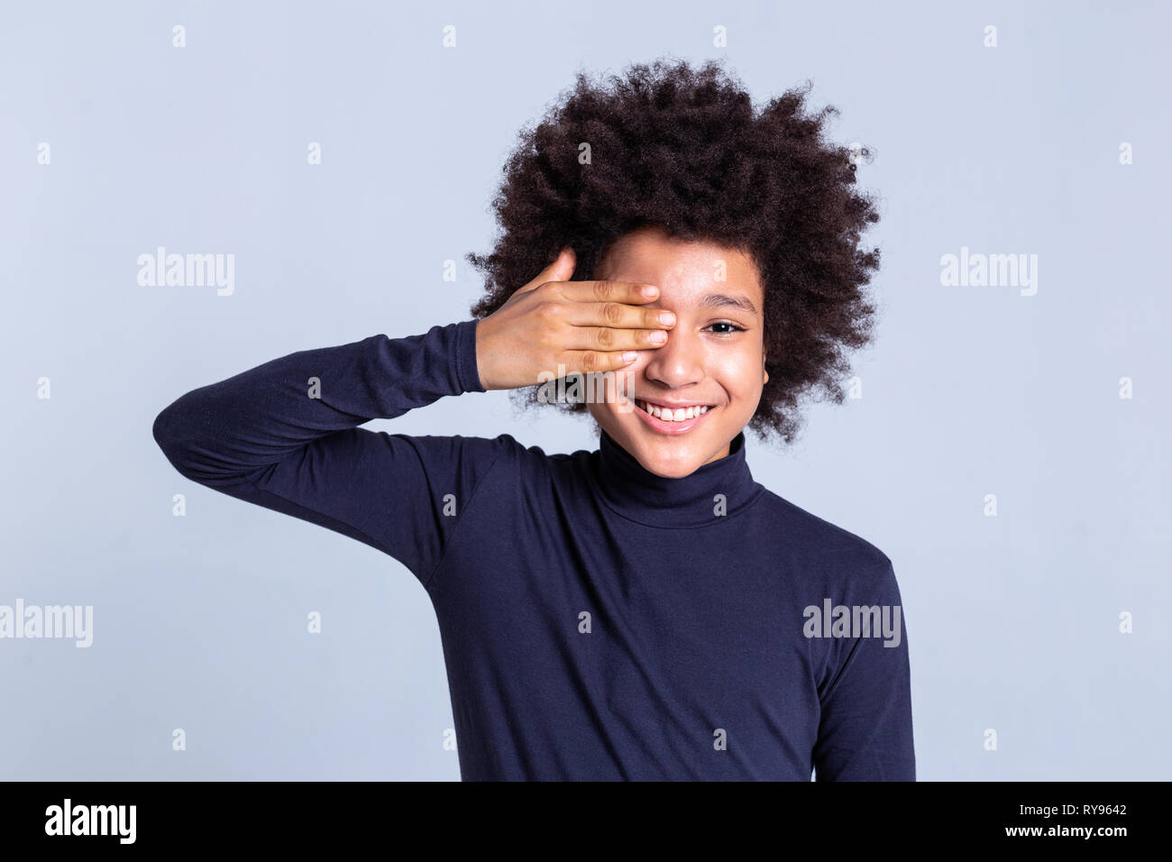 Smiling curly positive child closing one eye with hand Stock Photo - Alamy