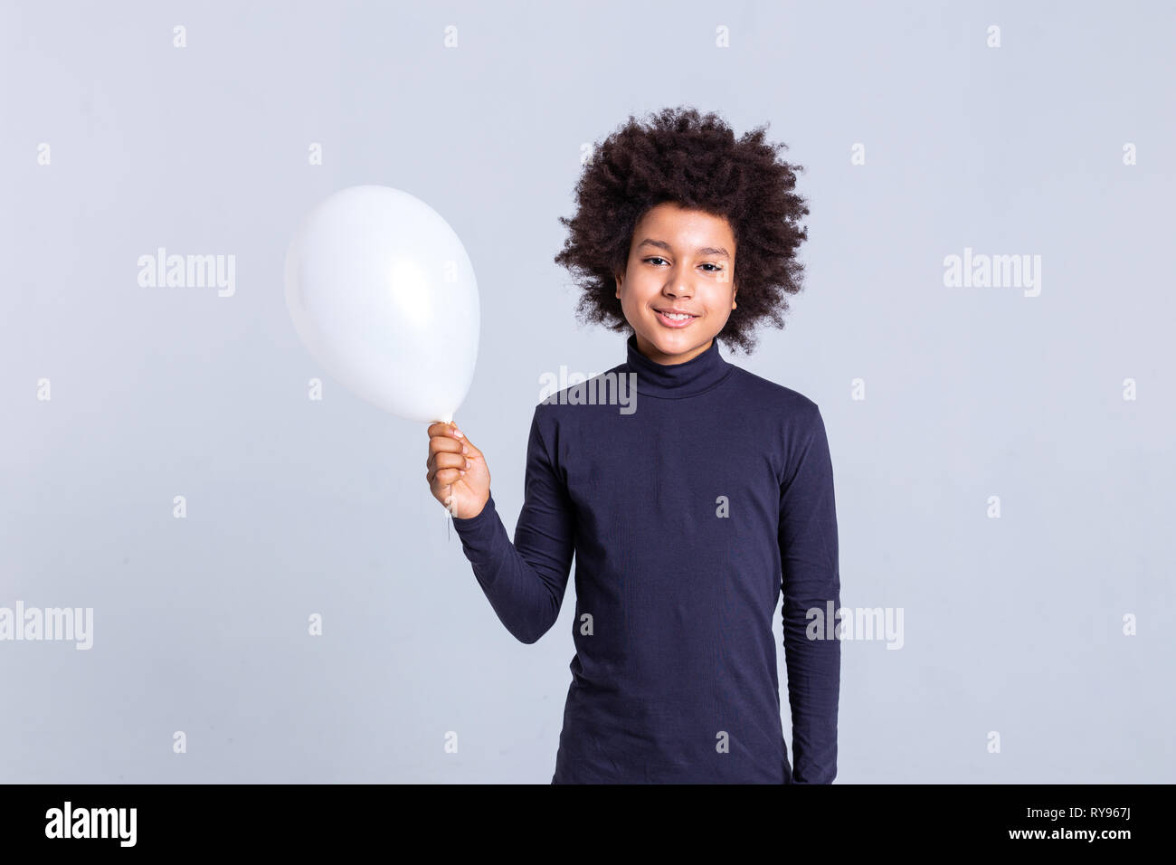 Beaming little boy standing on monochromic background and carrying ...