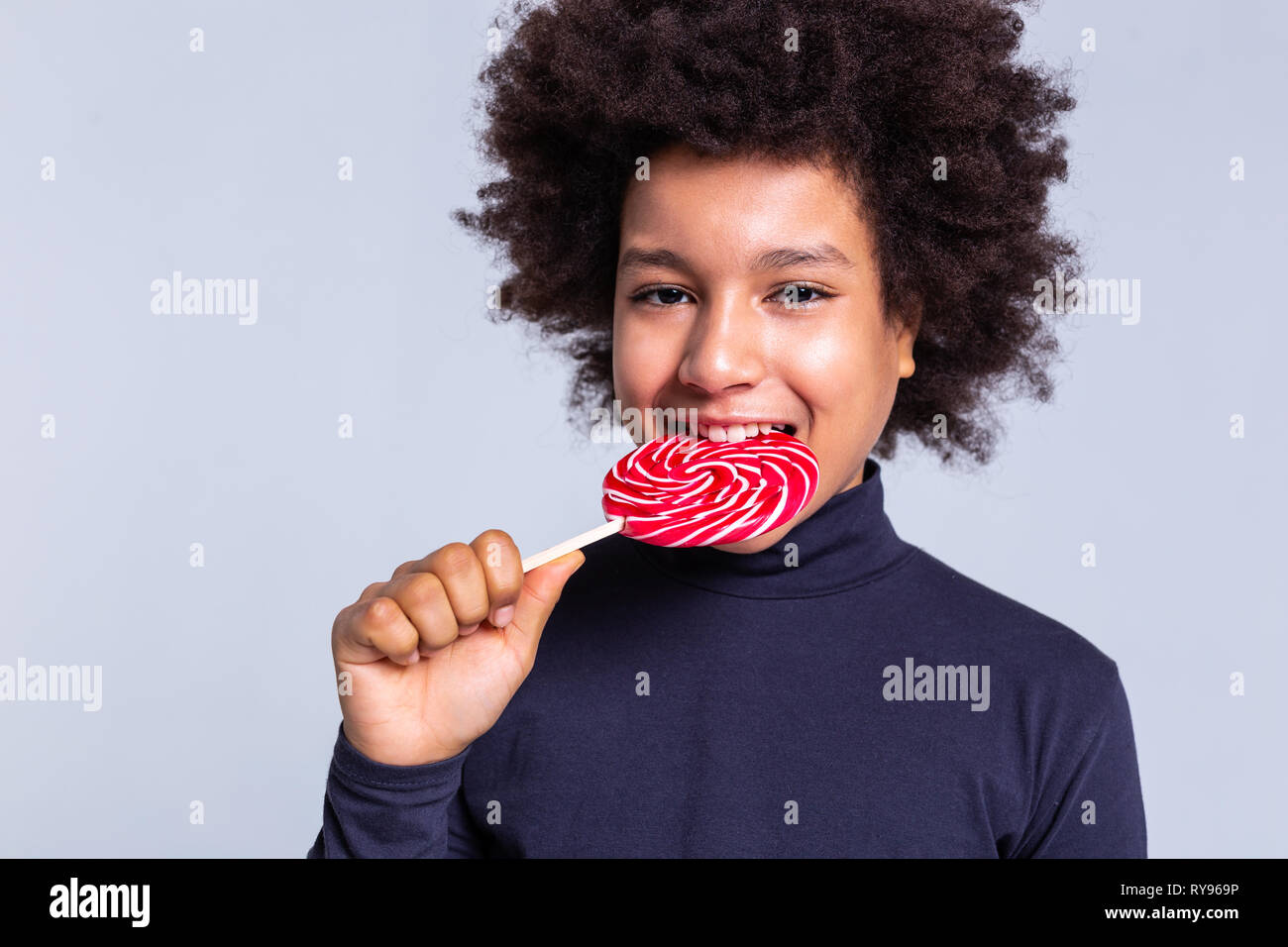 Cheerful African American child biting red sticky candy Stock Photo - Alamy