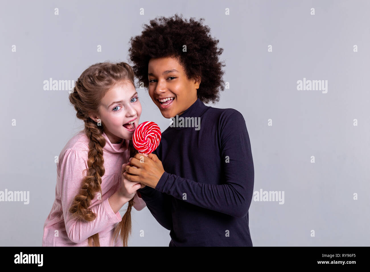 Beaming light-haired girl with big blue eyes licking red candy Stock ...