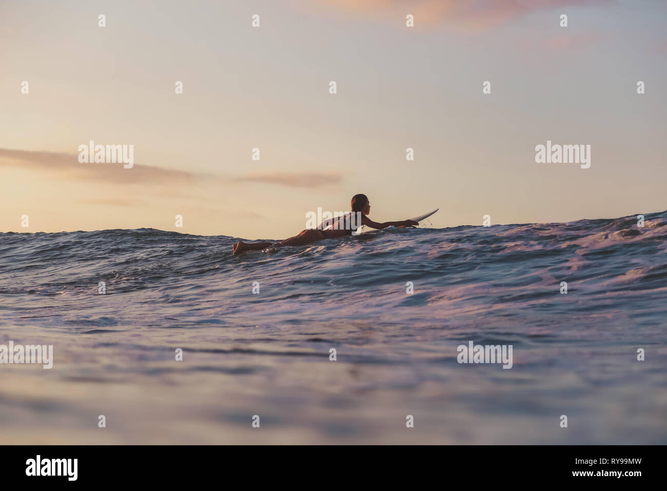Side view of cheerful female floating on surf board between water of ...