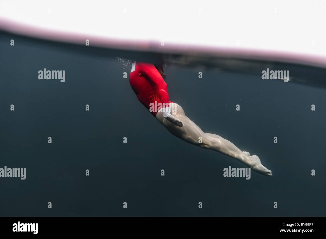 Side view of female in red swimsuit diving in blue water of sea on Bali ...