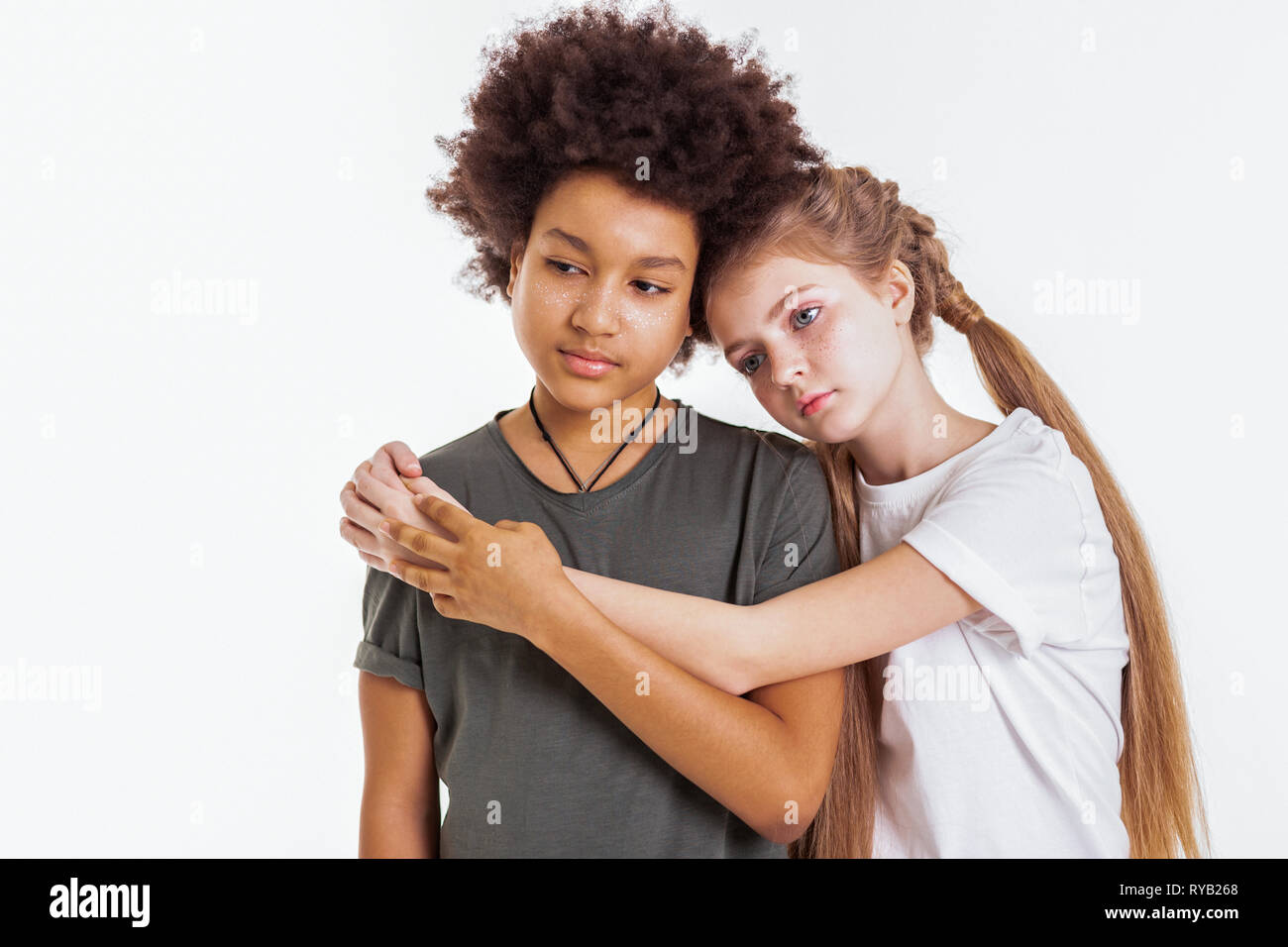 Emotionless pretty long-haired girl hugging her African American friend ...
