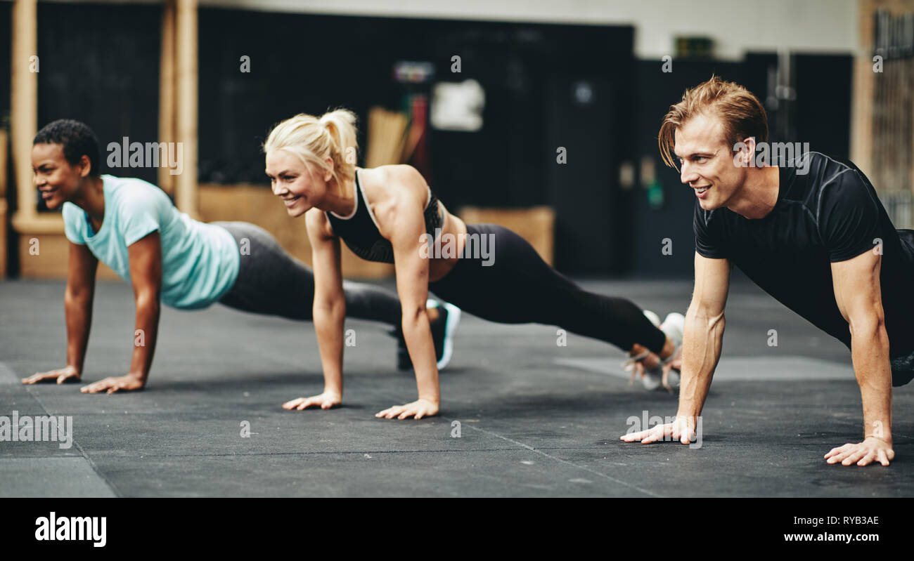 Diverse group of smiling young people in sportswear doing pushups ...