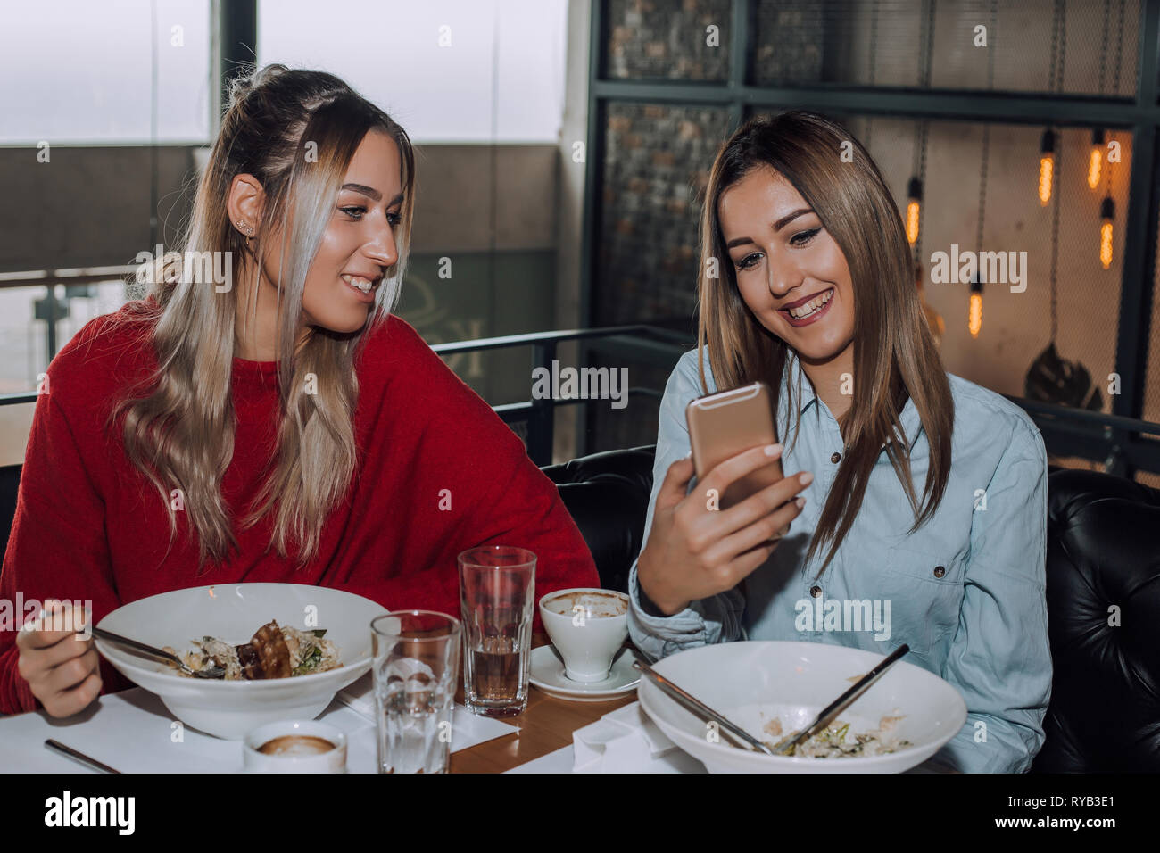Two young women using a mobile phone during lunch in a restaurant ...