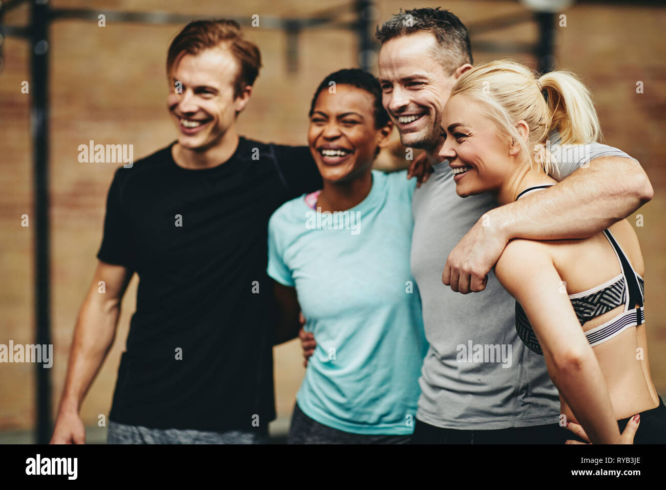 Diverse group of laughing friends in sportswear standing arm in arm in ...