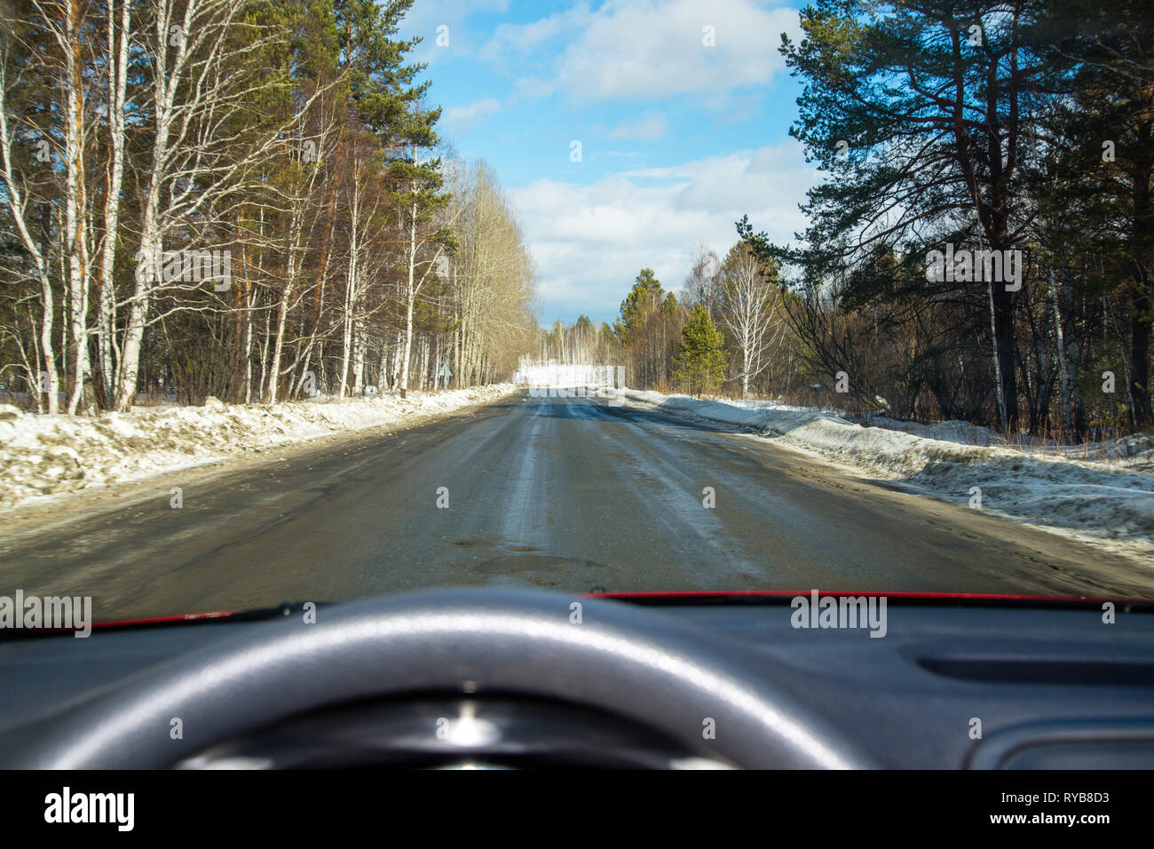 Spring forest wet road from the window of the car. Blue sky with clouds ...
