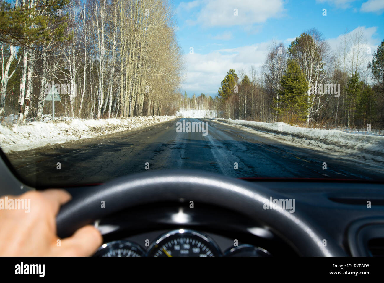 Spring forest wet road from the window of the car. Blue sky with clouds ...