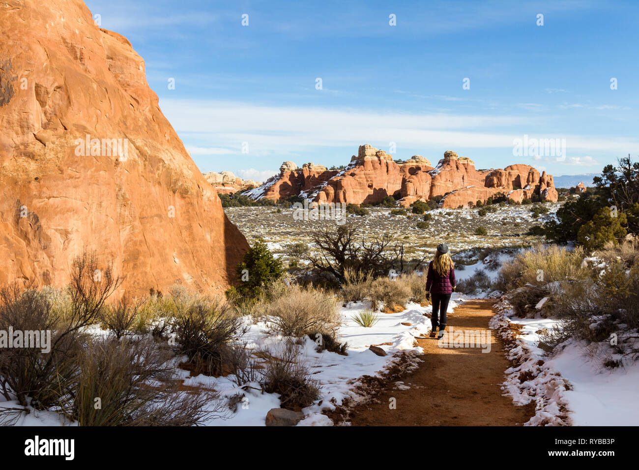 woman hiking on the red sandstone trail surrounded with fresh snow with ...