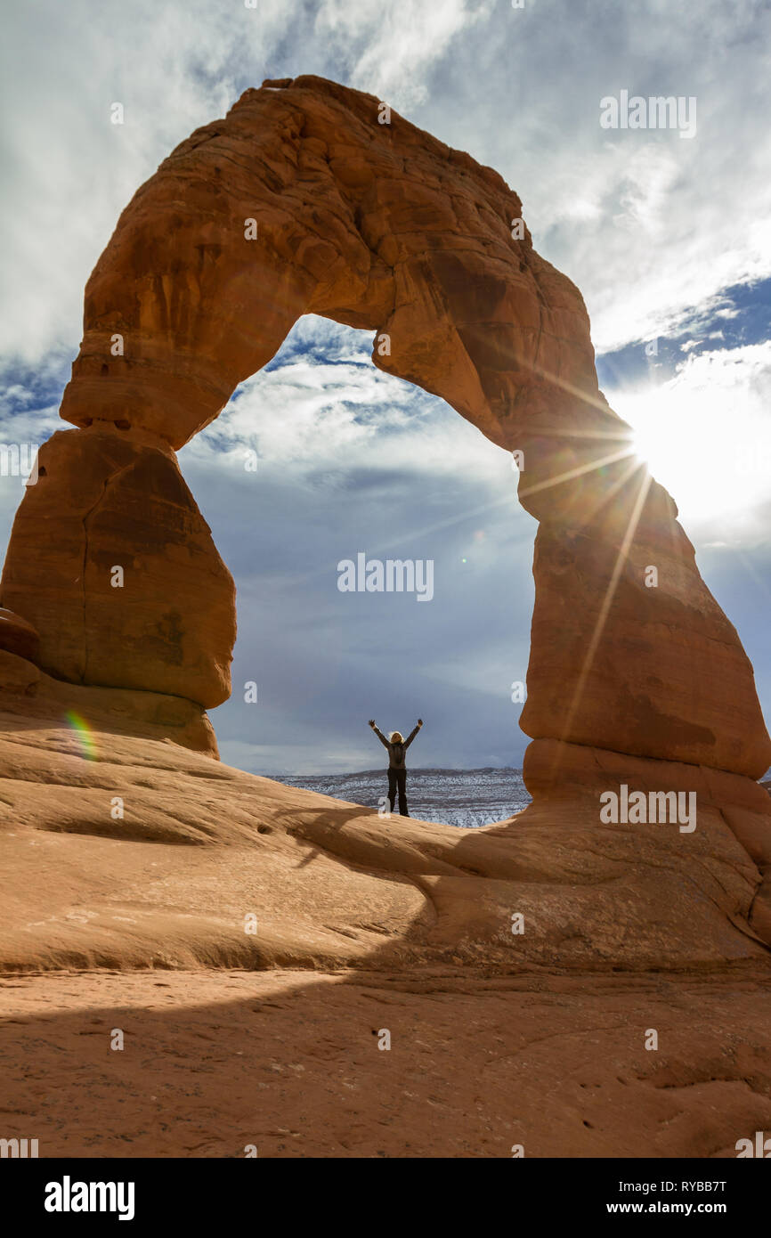 Delicate arch in the winter with a hiker standing at the base of to ...