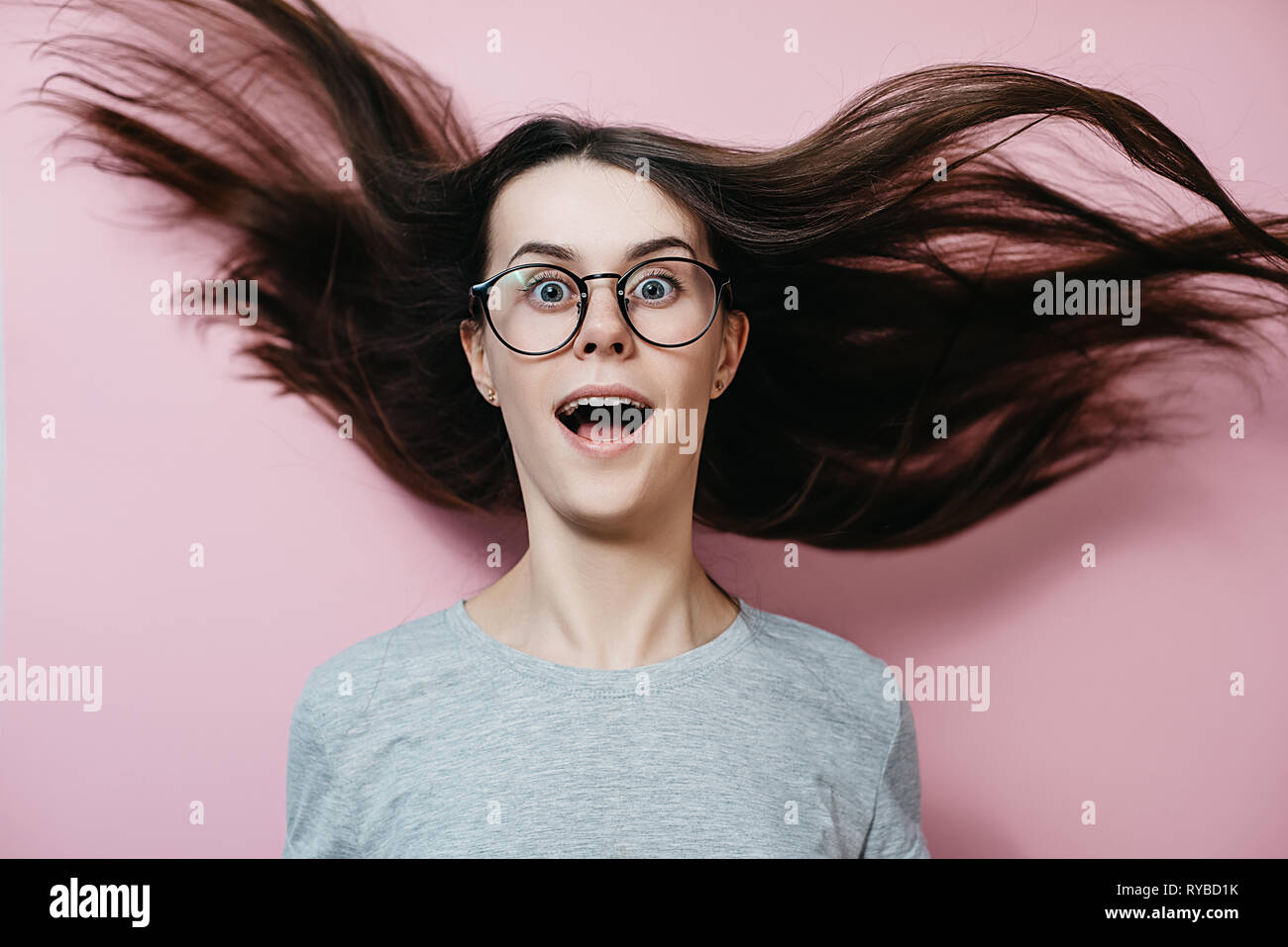 Young girl in glasses with flying hair in panic looks with surprised ...