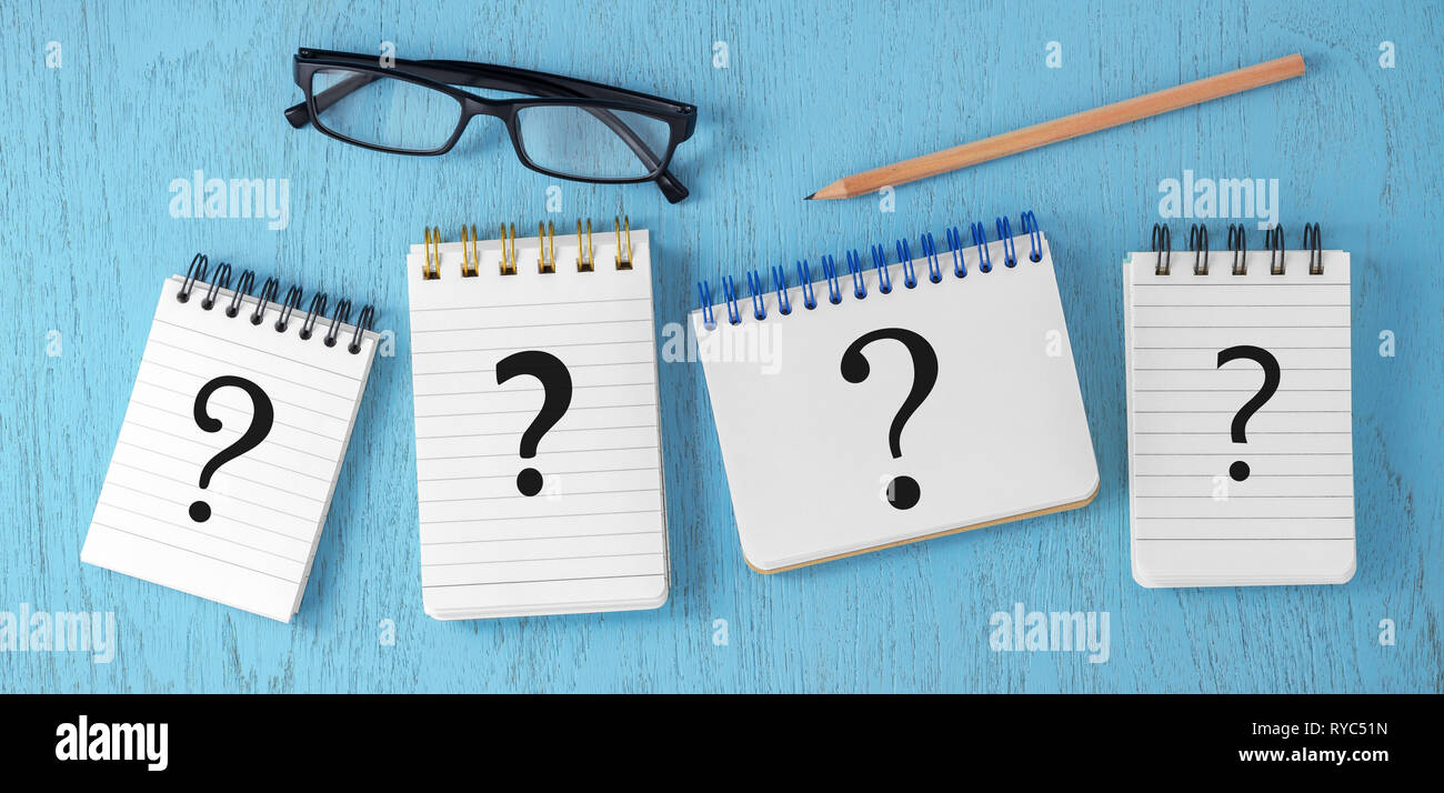 Question marks on notepads on blue wooden desk, variety of questions ...
