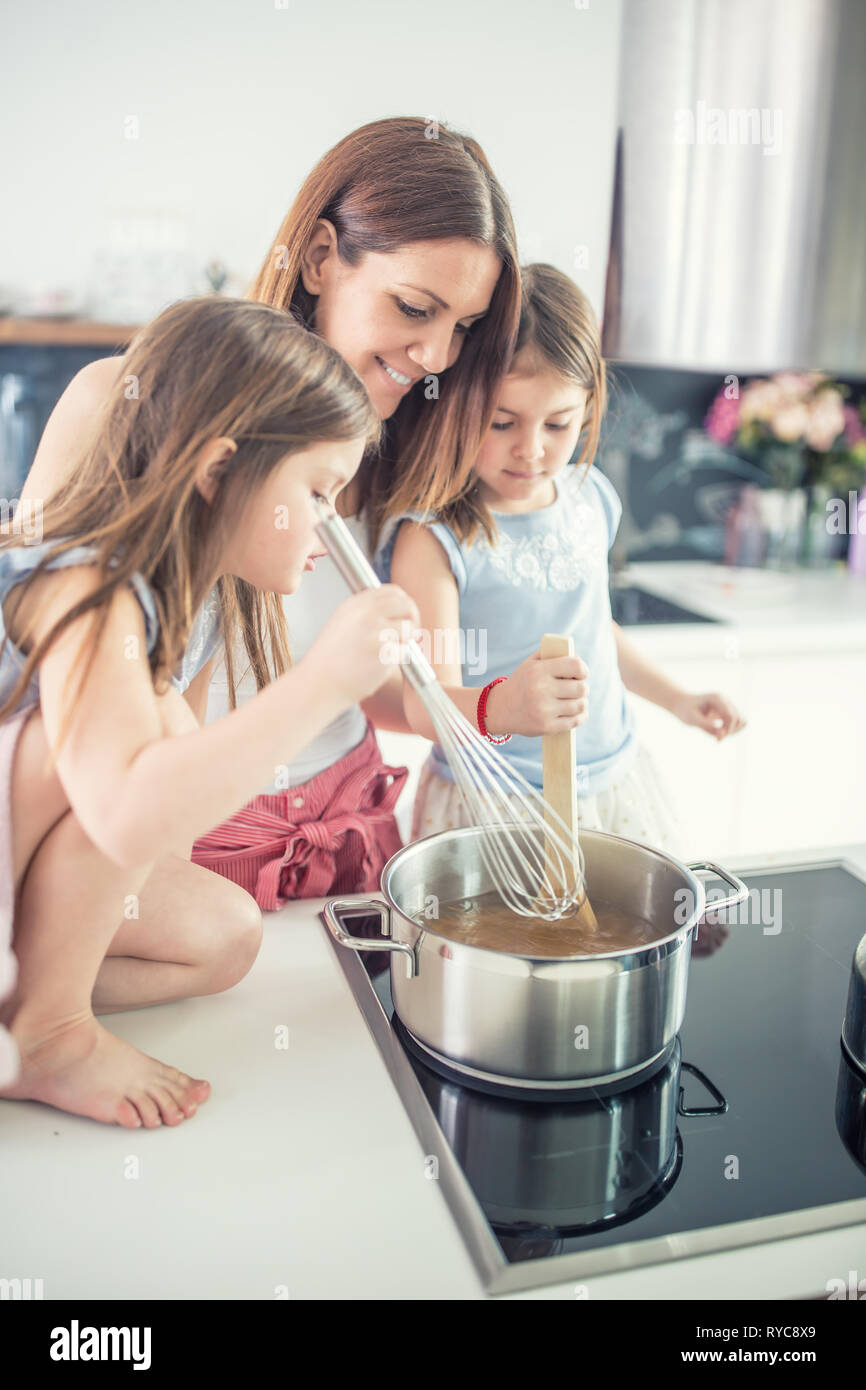 Mom with two young twins daughters in the kitchen cooking spaghetti ...