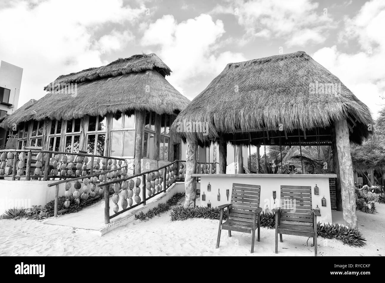 exotic beach bar with house building and straw roof near chairs on sand ...