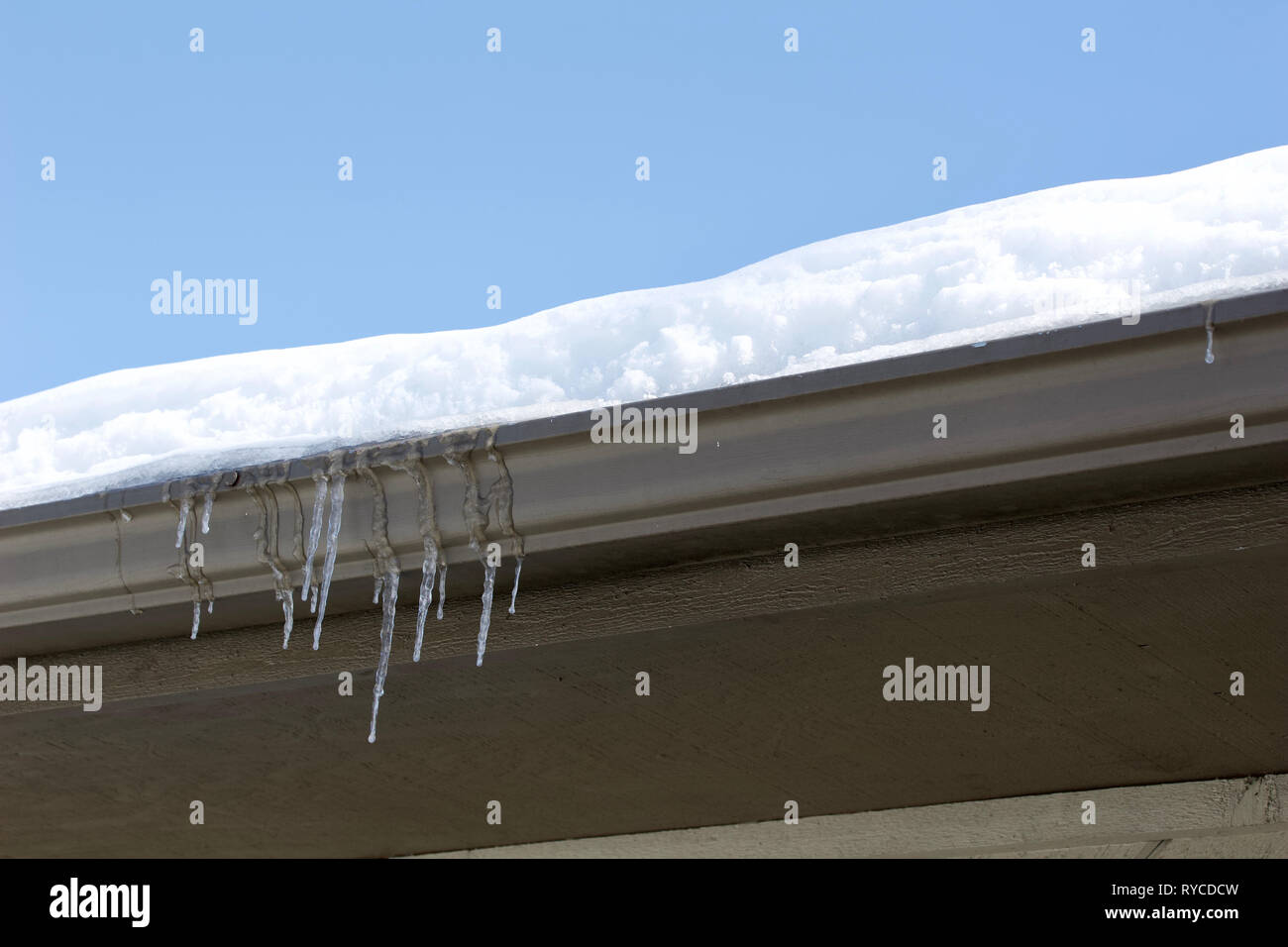Close upward view of Icicles dripping from a snow filled roof rain ...