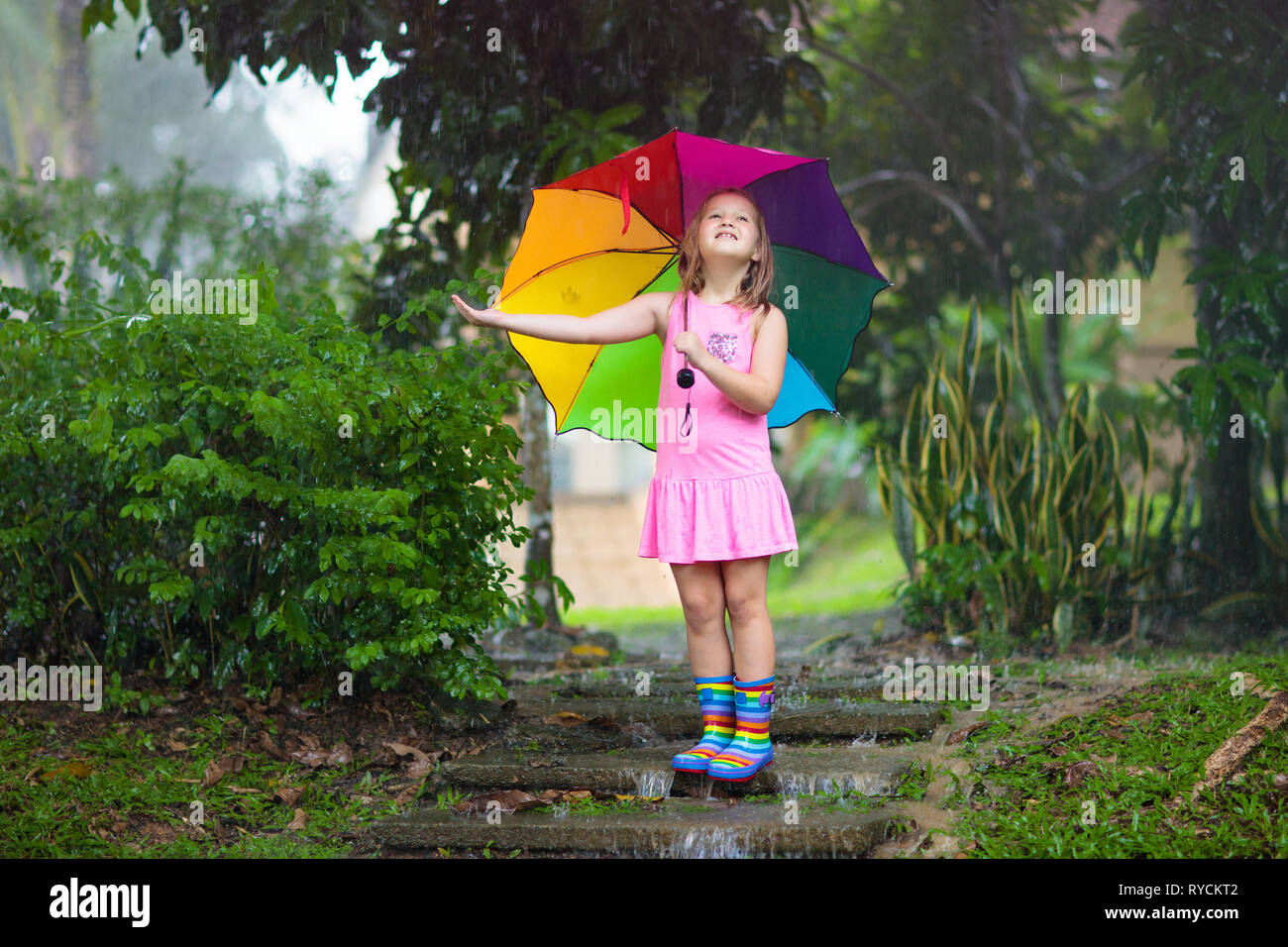 Kid playing out in the rain. Children with umbrella and rain boots play ...