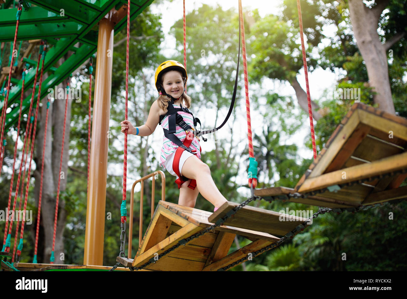 Child in forest adventure park. Kids climb on high rope trail. Agility ...