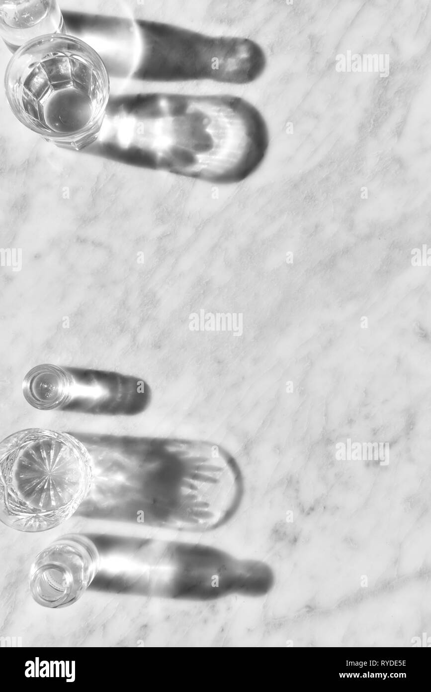 A glass of water in sunlight with strong shadows cast on a marble ...