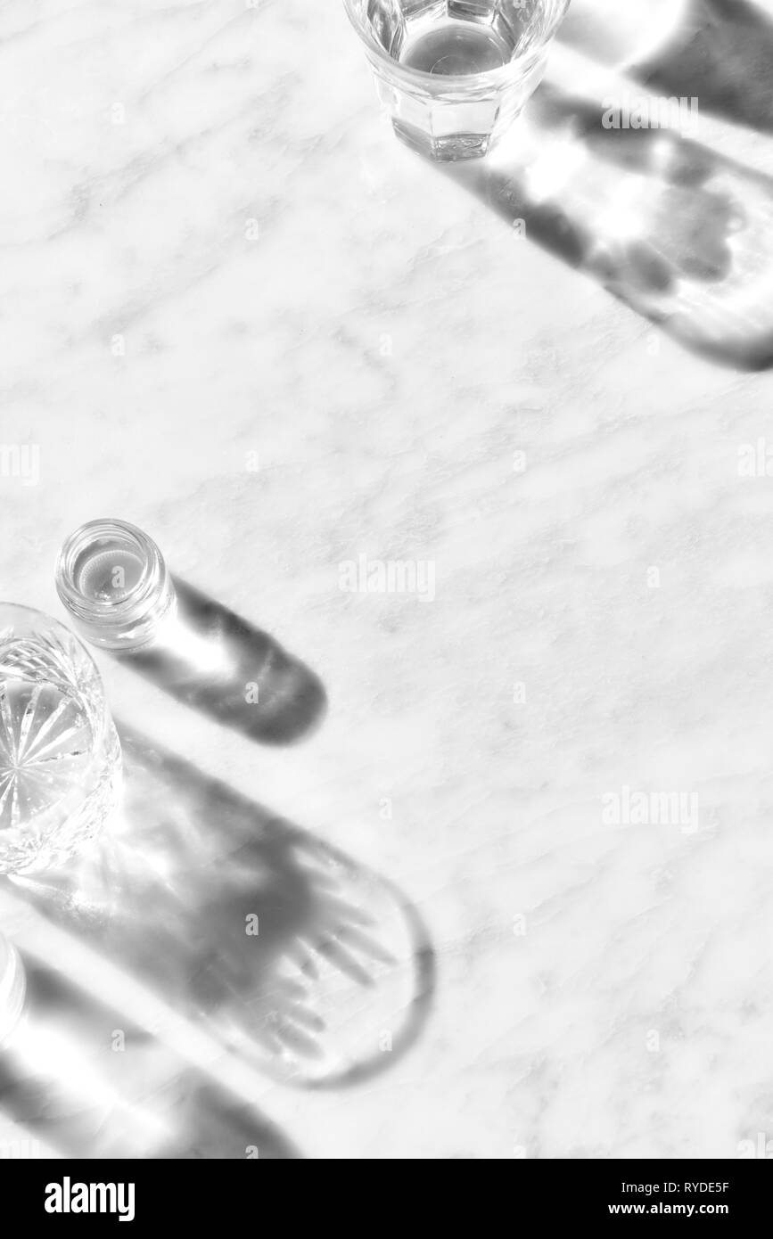 A glass of water in sunlight with strong shadows cast on a marble ...