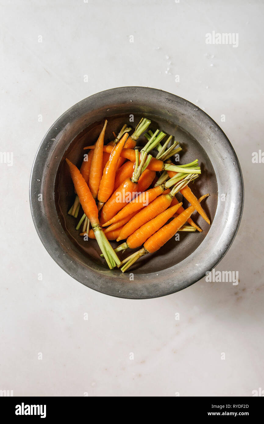 Young mini carrot in water in vintage metal bowl over white marble ...