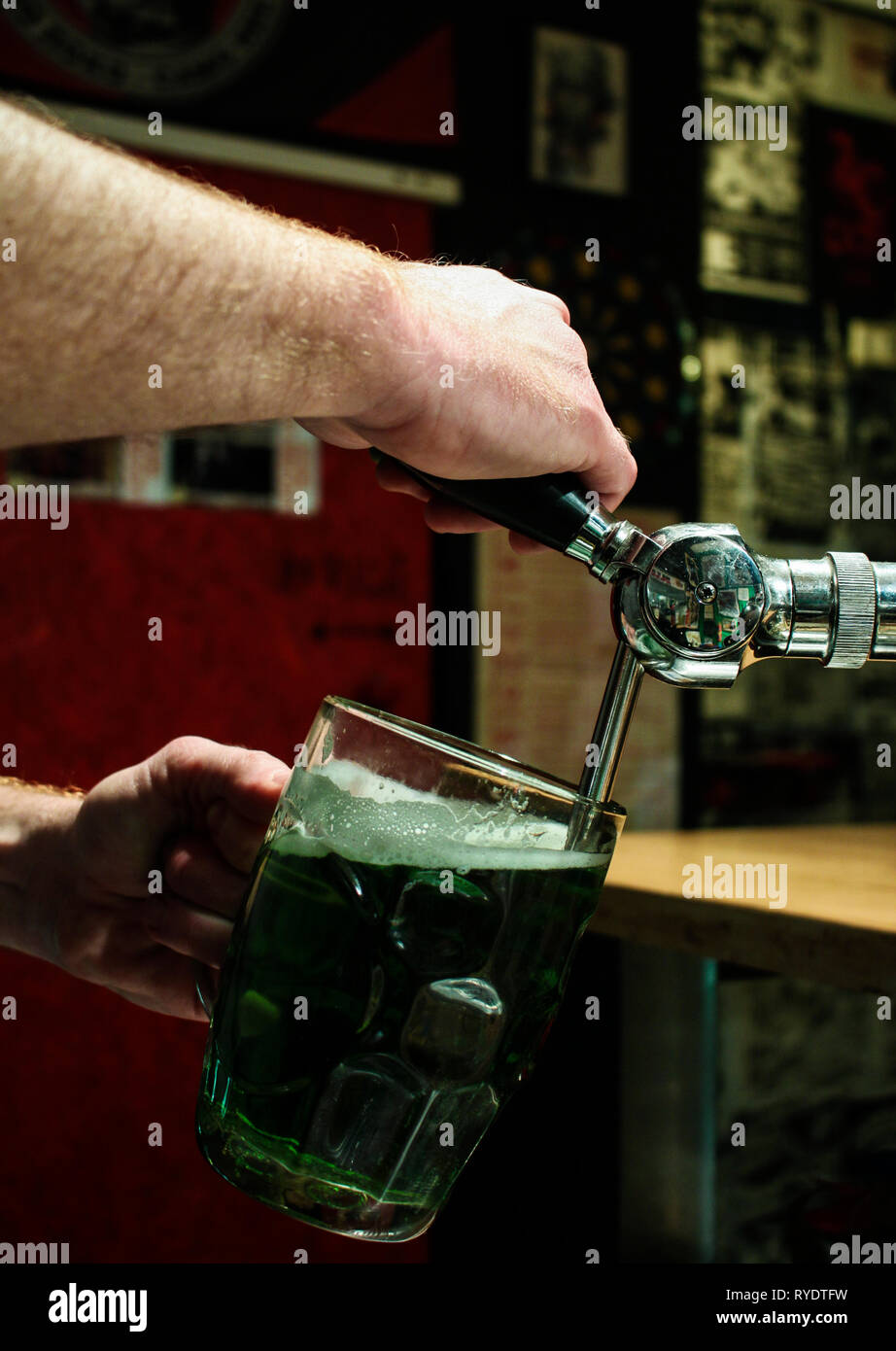 Pouring green beer in glass jug by bartender in Irish pub or some other ...