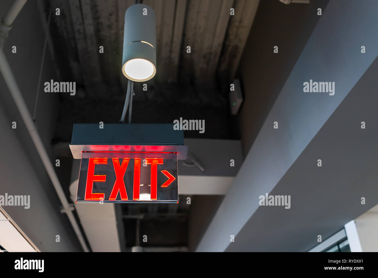 Red exit sign hanging from ceiling looking up view with arrow direction ...