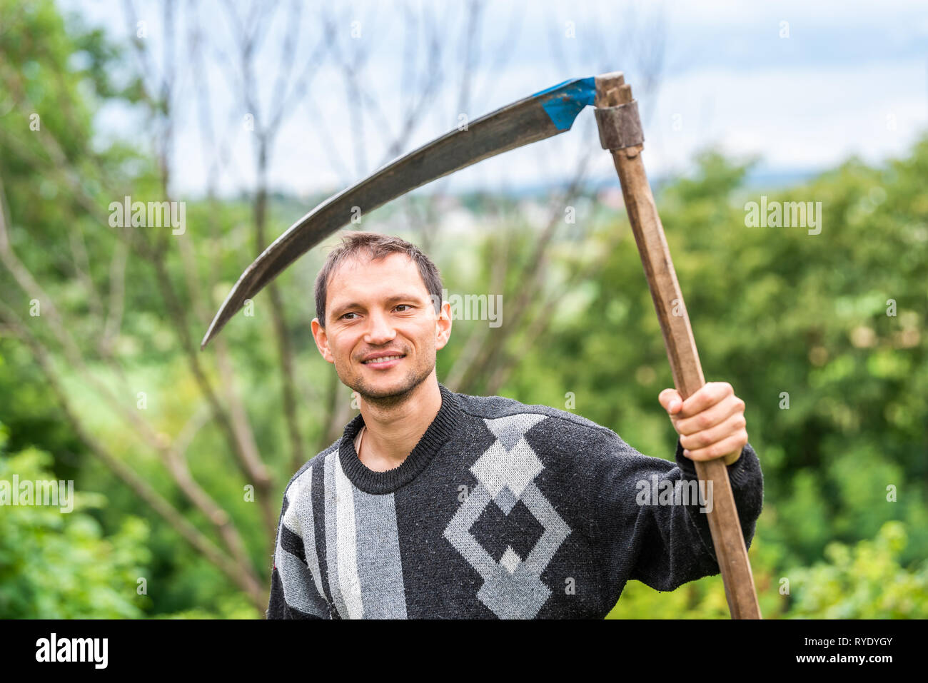 Happy young man closeup face farmer in garden standing with sickle ...