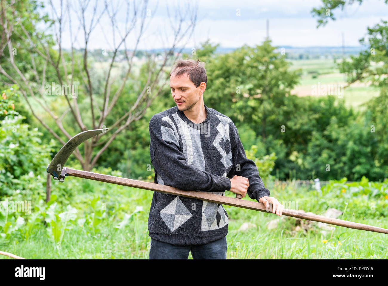 Young man farmer in garden standing with sickle scythe tool in green ...